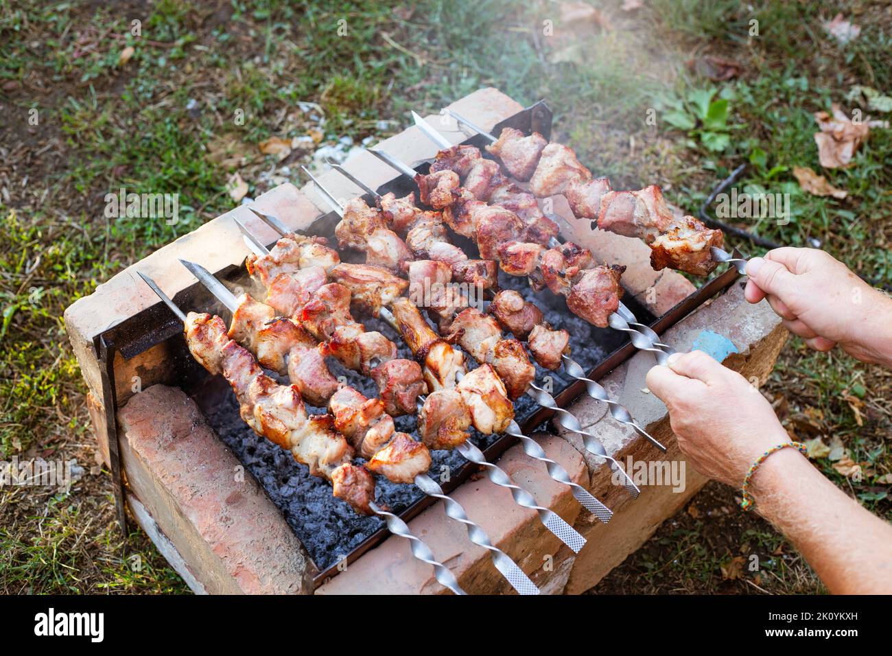 A man flips pork skewers grilled over coals on a brick grill. Delicious ...