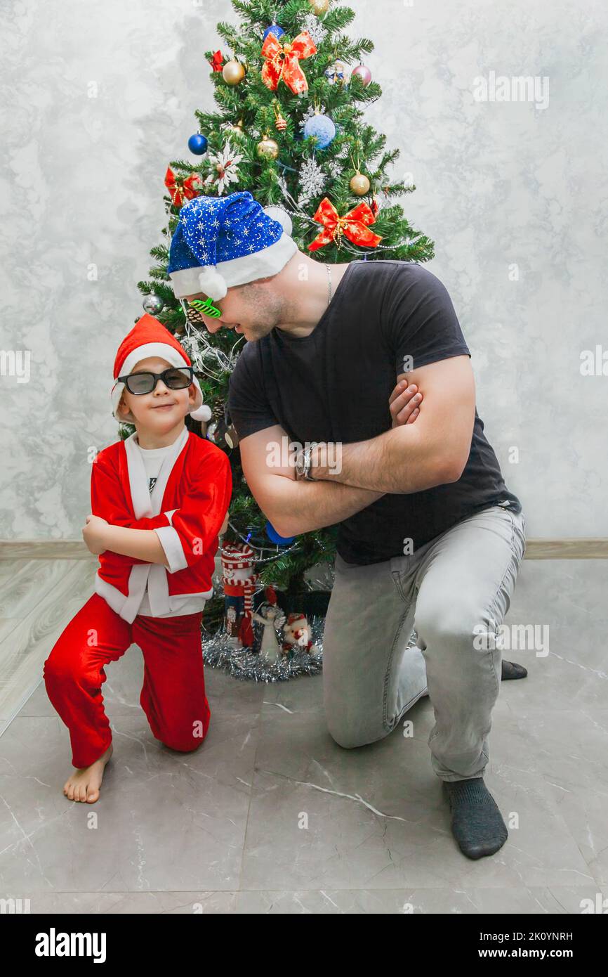 A boy in a Santa suit and his dad in funny sunglasses are on one knee ...