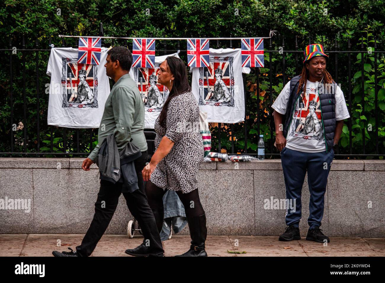 Two people pass by a man selling t-shirts of Queen Elizabeth II shortly ...