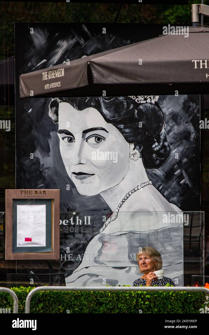 A lady drinks tea at a cafe in front of a painting of Queen Elizabeth ...