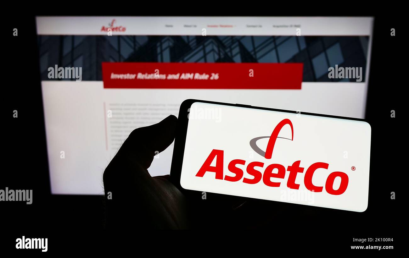 Person holding cellphone with logo of British financial services company AssetCo plc on screen ...
