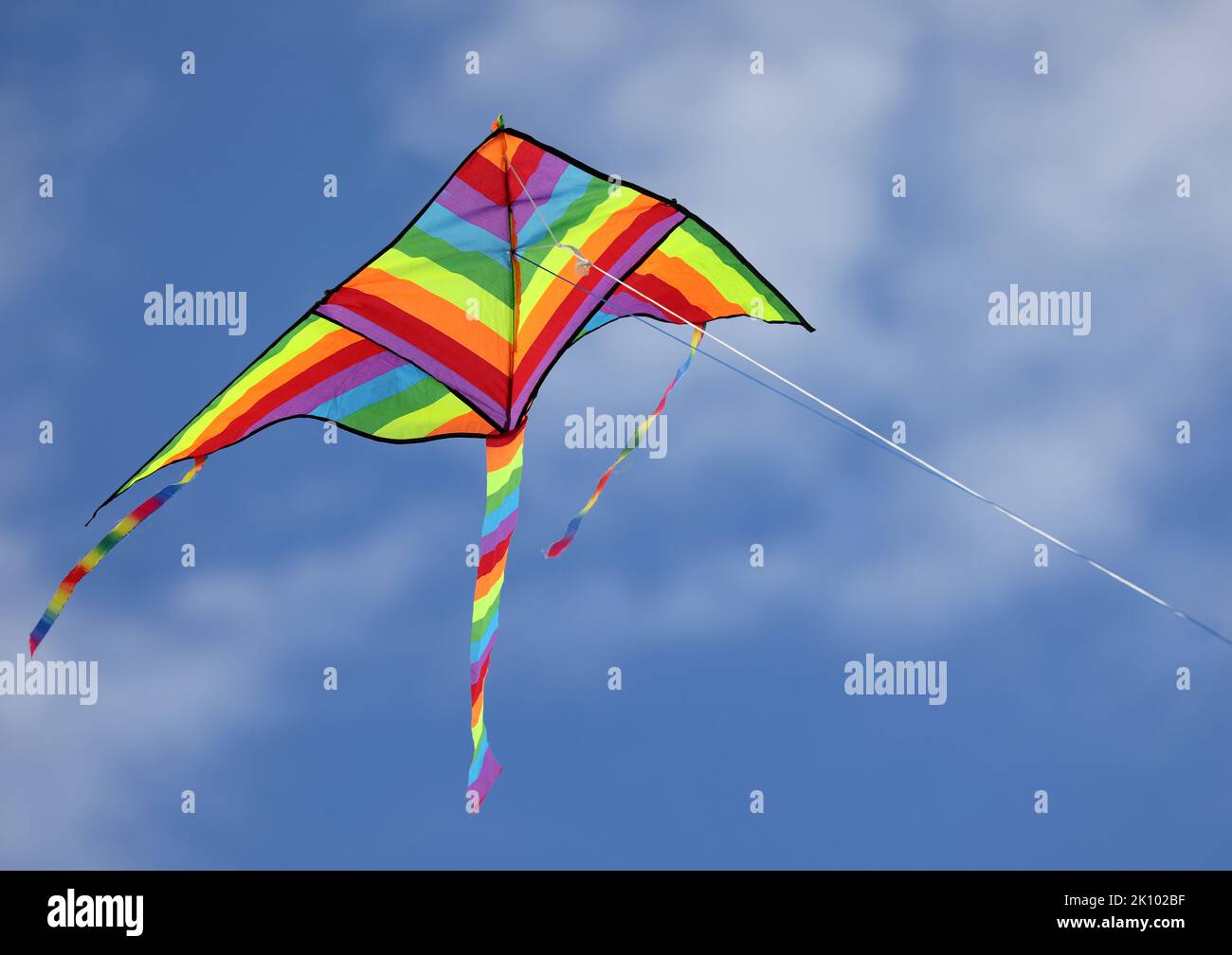 large kite with the many colors of the rainbow flying high attached to ...