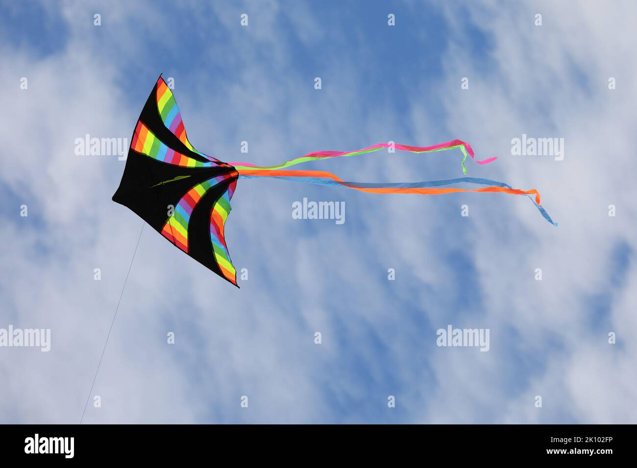 big kite with black color and many colors of the rainbow flying high ...