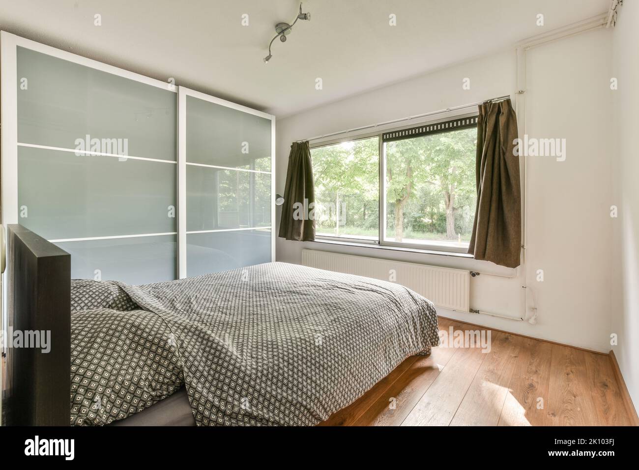 Comfortable bed with blanket and pillows located near sliding wardrobe ...