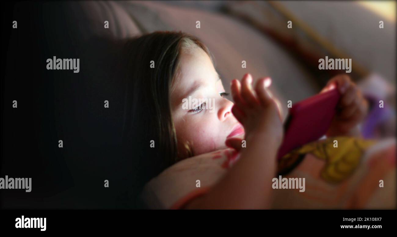 Small girl looking at cellphone screen. Smartphone light glow on child ...