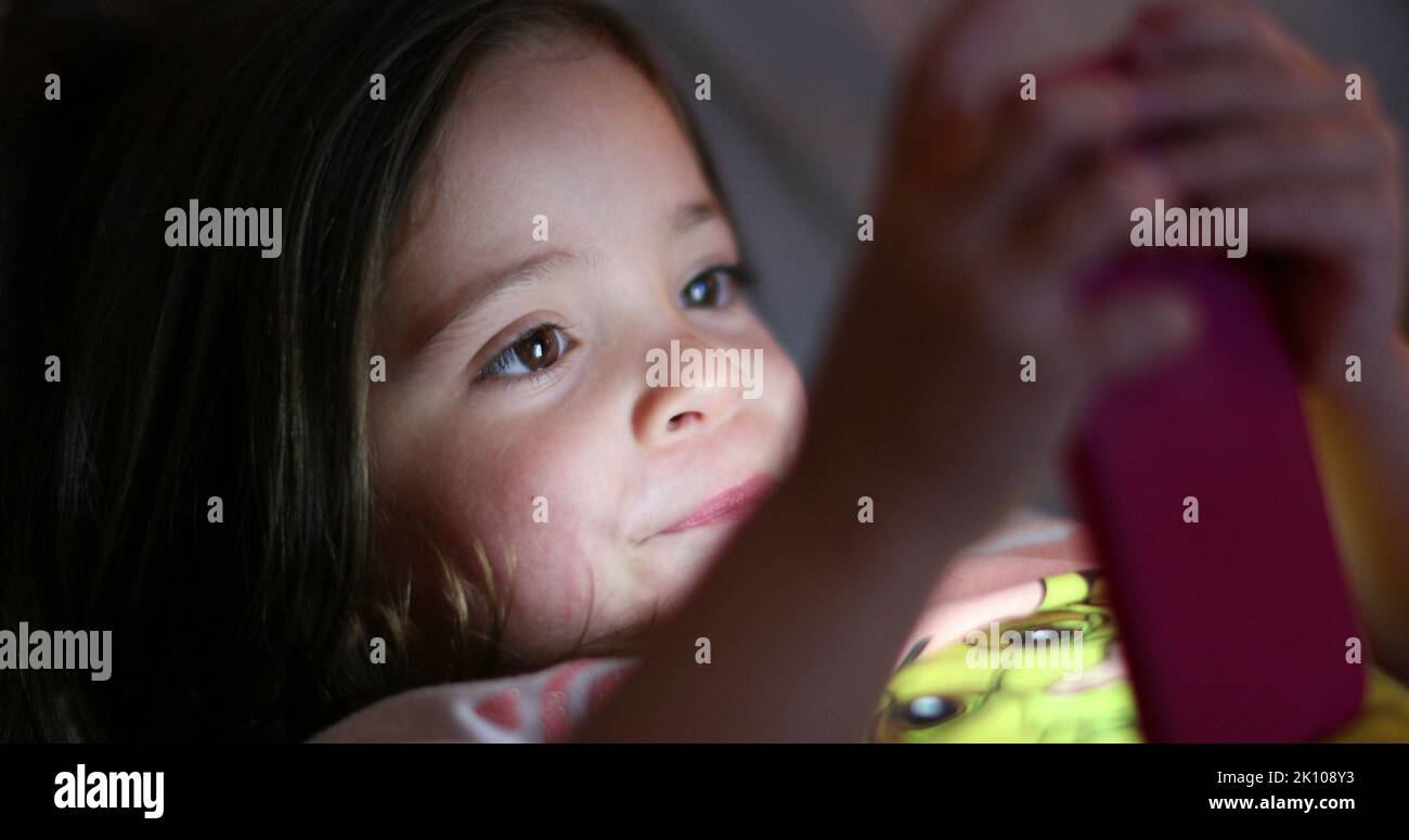 Little girl child using smartphone device. Light glowing on girl face ...