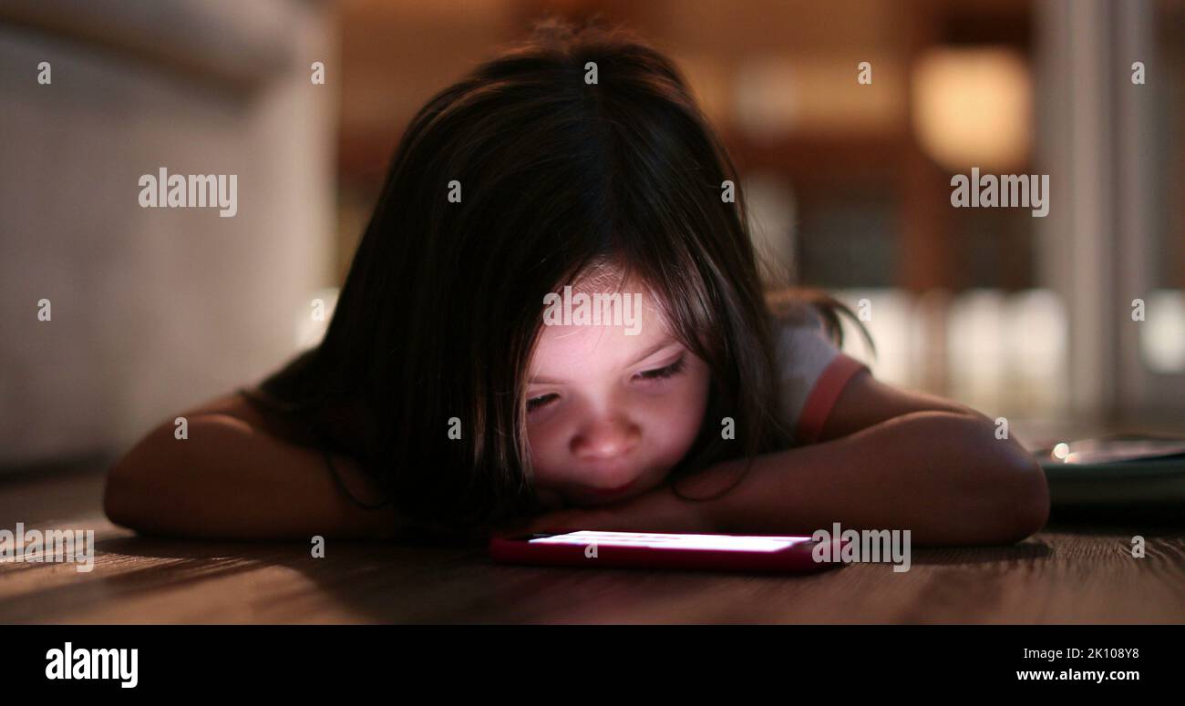 Small girl staring at cellphone screen at night. Cute kid lying on ...