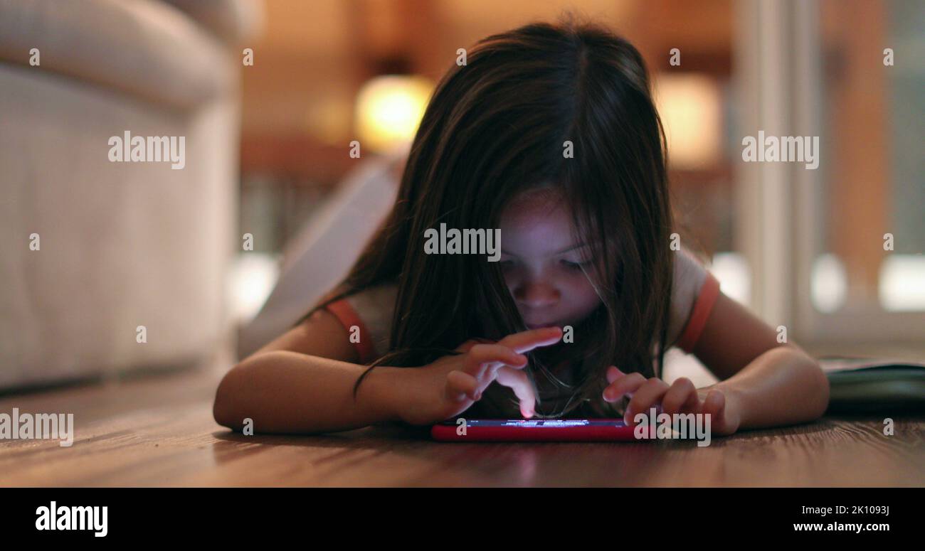 Little girl using cellphone device at night at home. Child staring at ...
