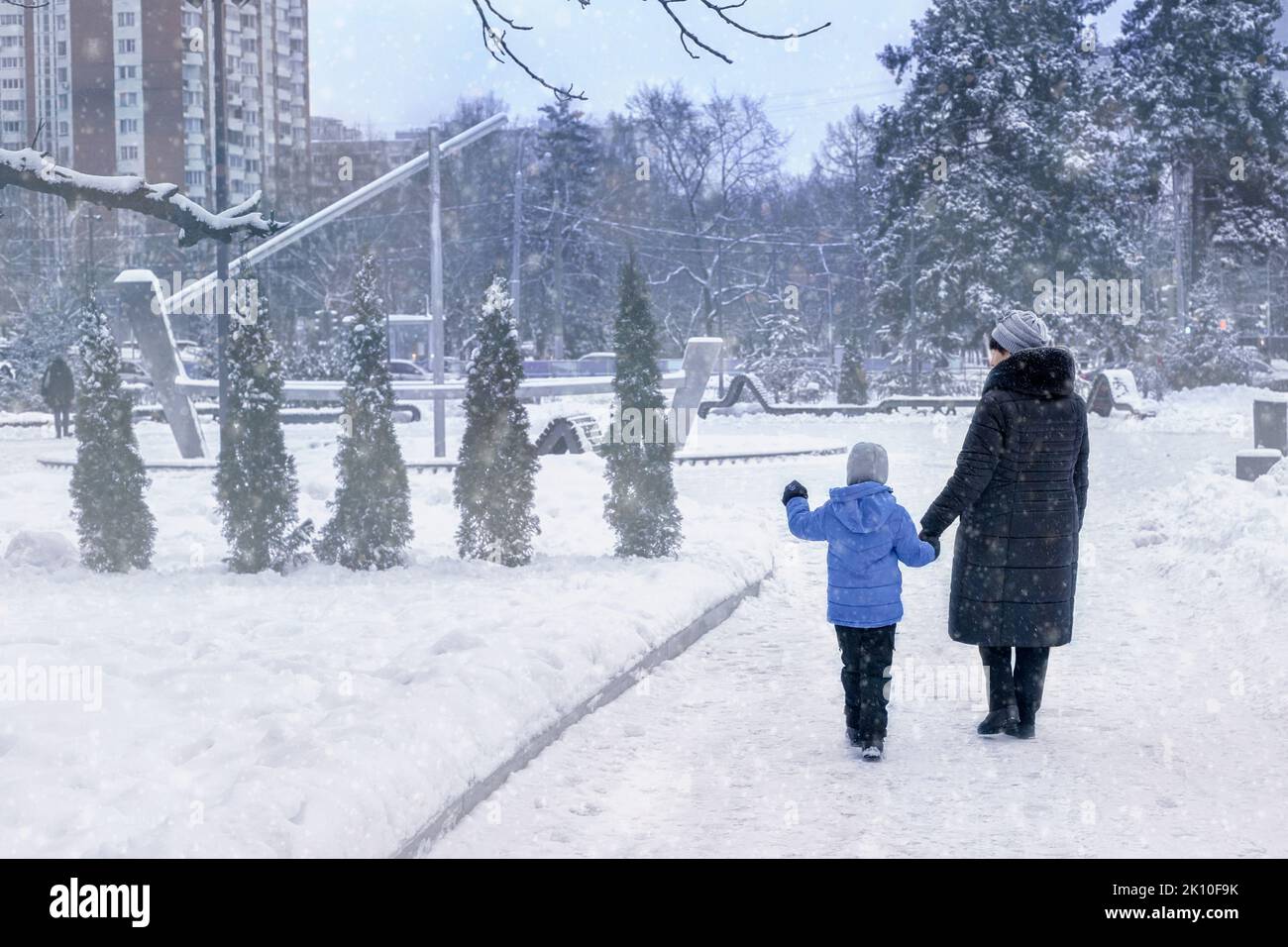 grandmother and grandson walk through the snow-covered city in winter ...