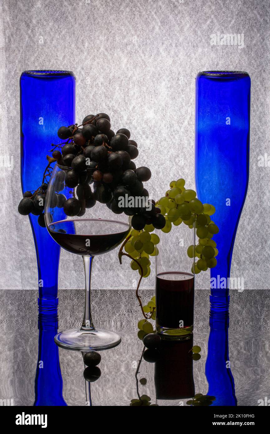 Still life with wine in glasses, grapes and inverted blue bottles Stock ...