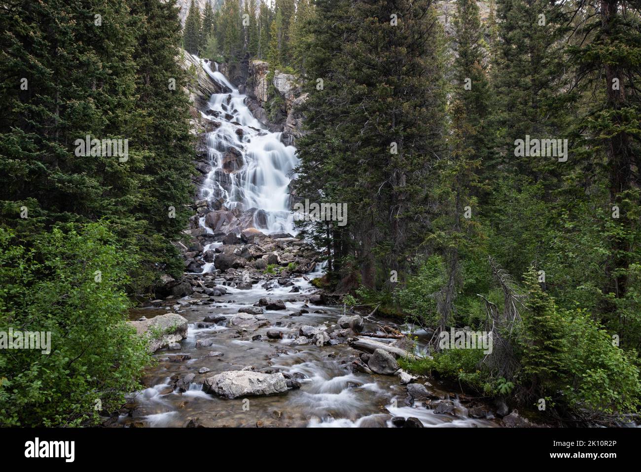 Hidden Falls pouring over large rocky cliffs through a forest at the mouth of Cascade Canyon ...