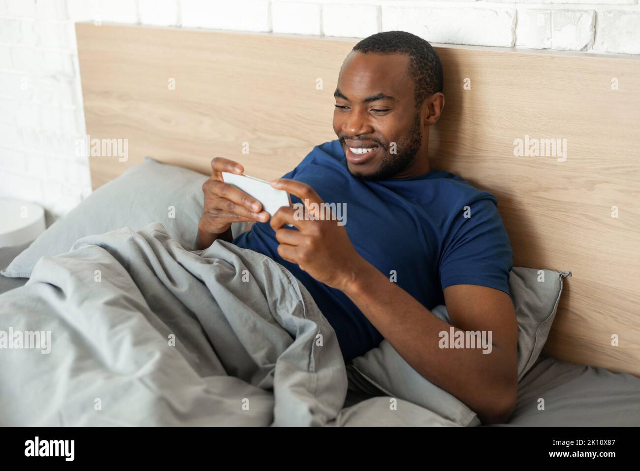 Cheerful African Guy Using Cellphone Playing Mobile Game In Bedroom ...