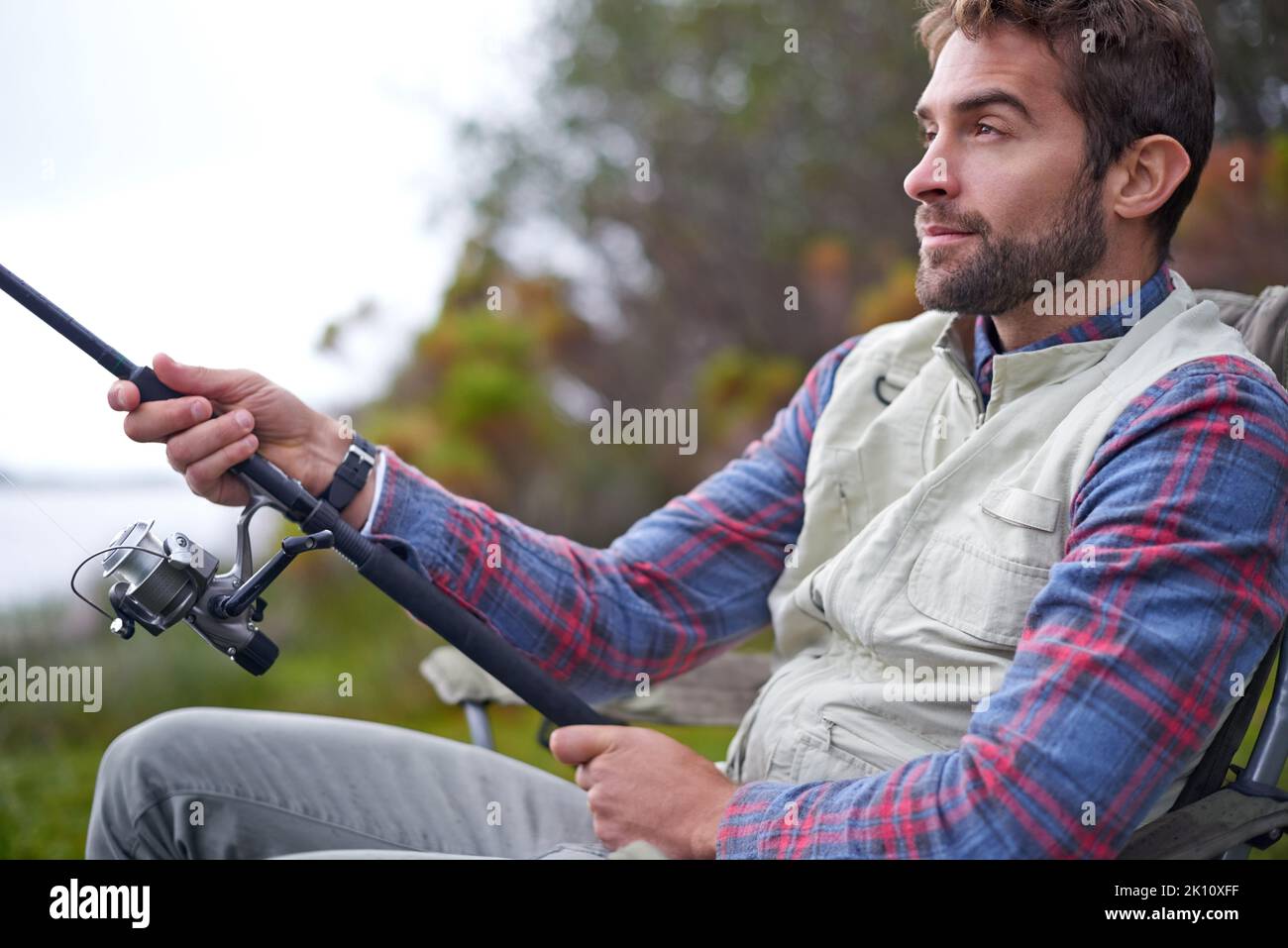 Getting away from it all. a handsome young man fishing by a lake Stock ...