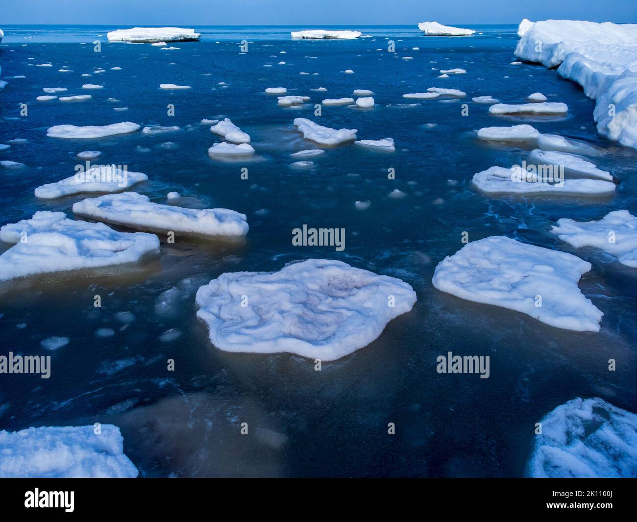 Melting ice blocks floating in dark sea water with frozen shore under ...
