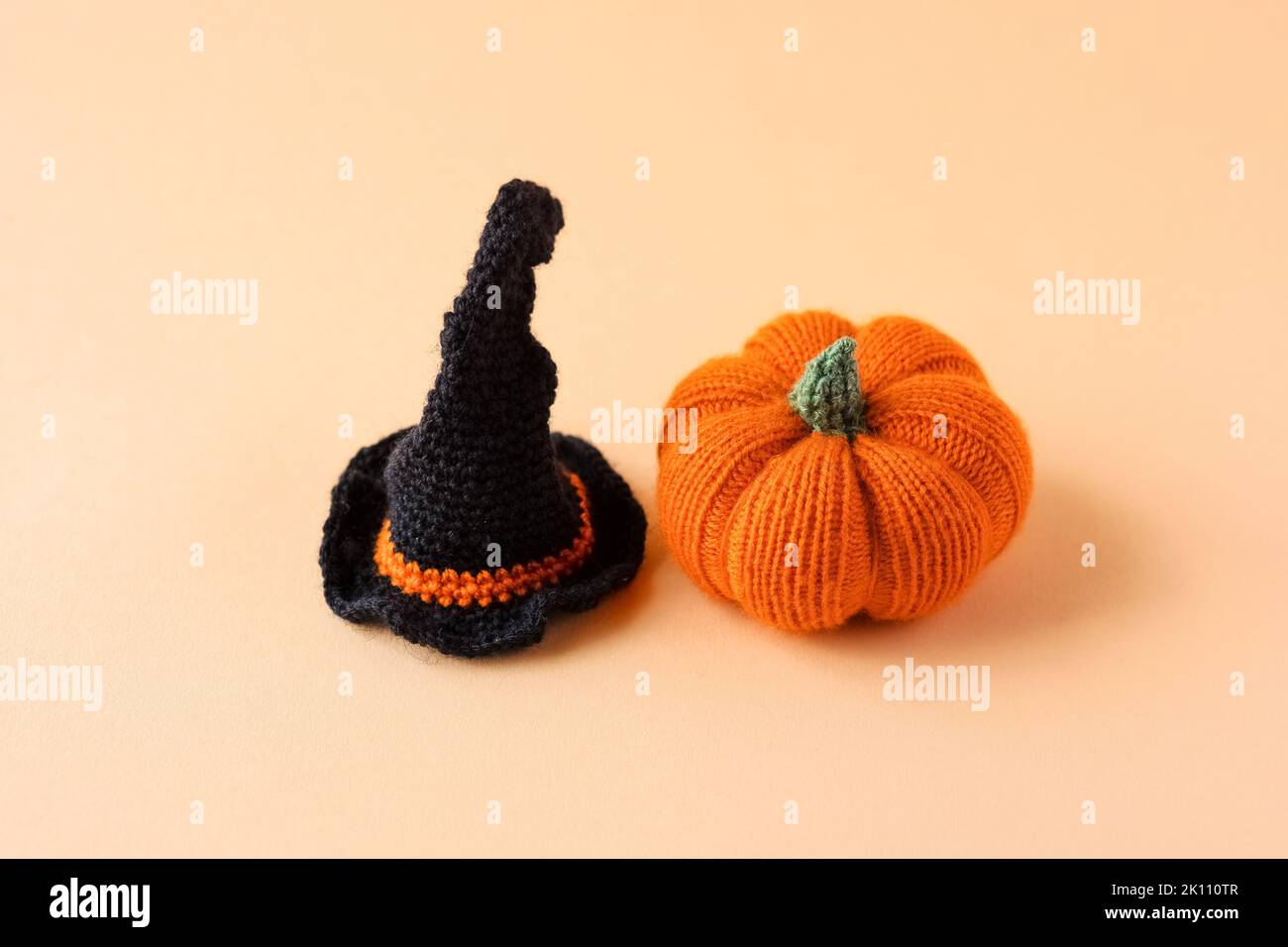 Knitted orange pumpkin with a black witch hat on an orange background ...