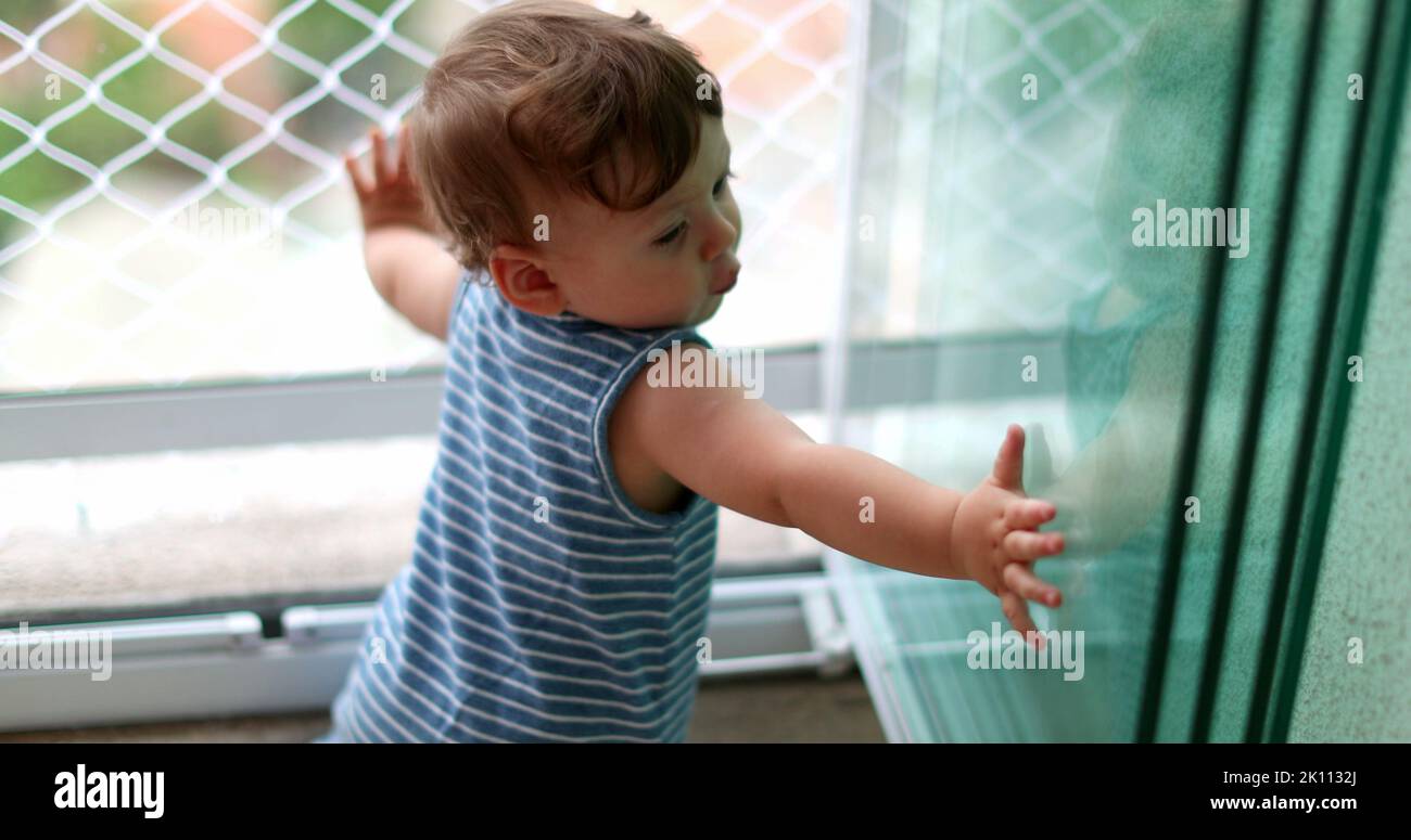 Baby standing by apartment window during lockdown, infant child ...
