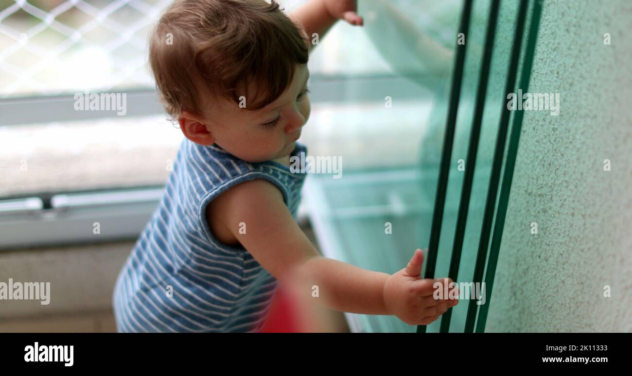 Baby standing by apartment window during lockdown, infant child ...