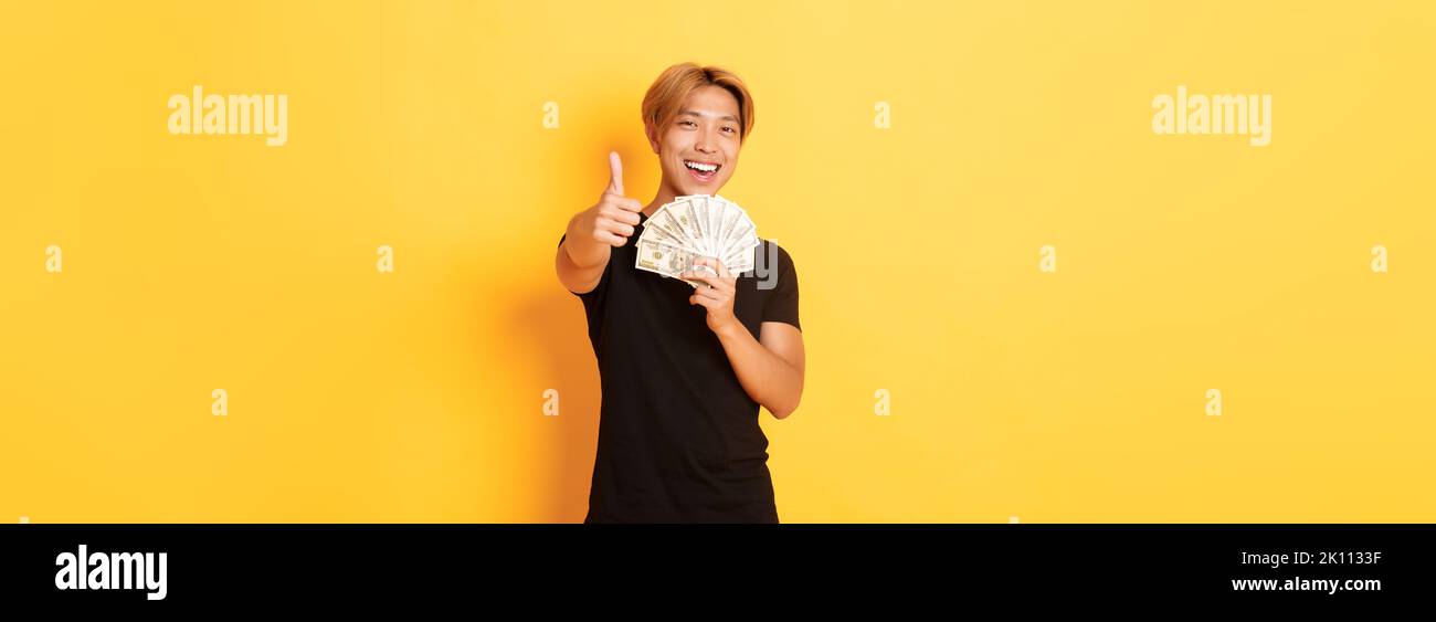 Portrait of handsome confident smiling asian guy showing thumbs-up and ...