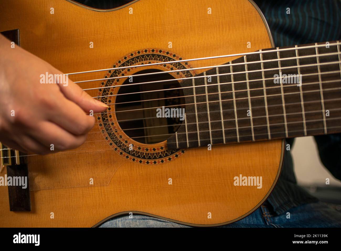 Hand of a musician with long nails playing a fret with eight strings ...