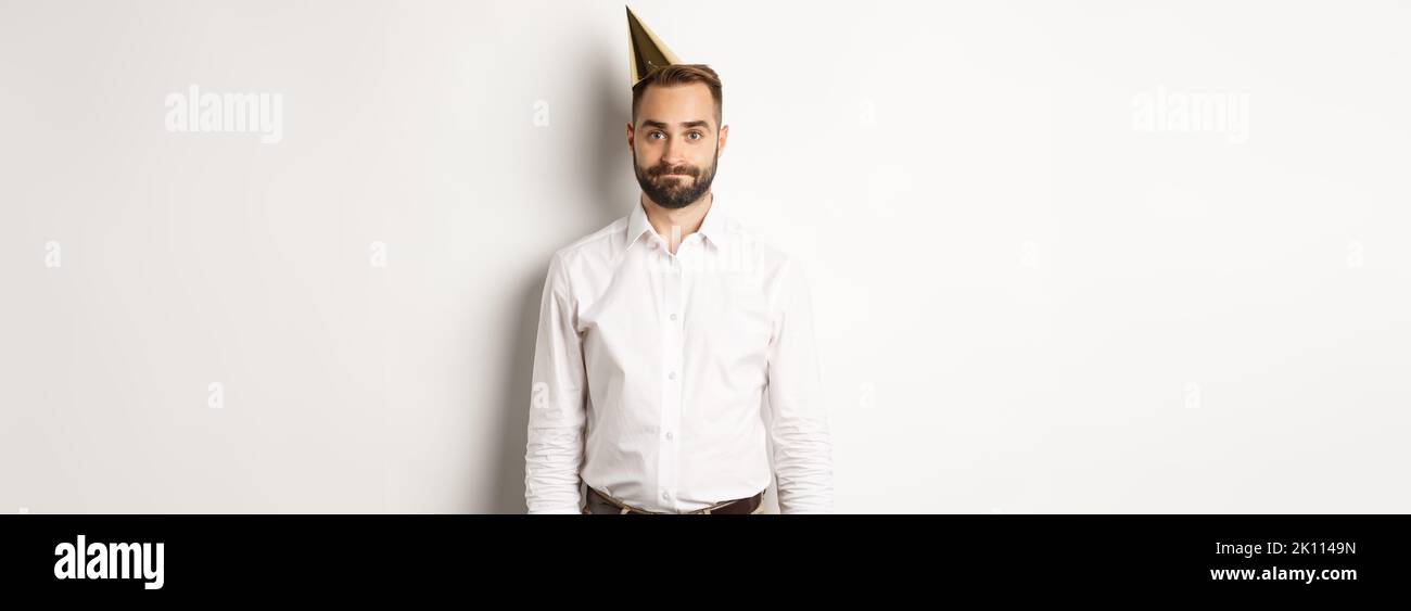 Celebration and holidays. Gloomy guy in birthday hat standing awkward ...