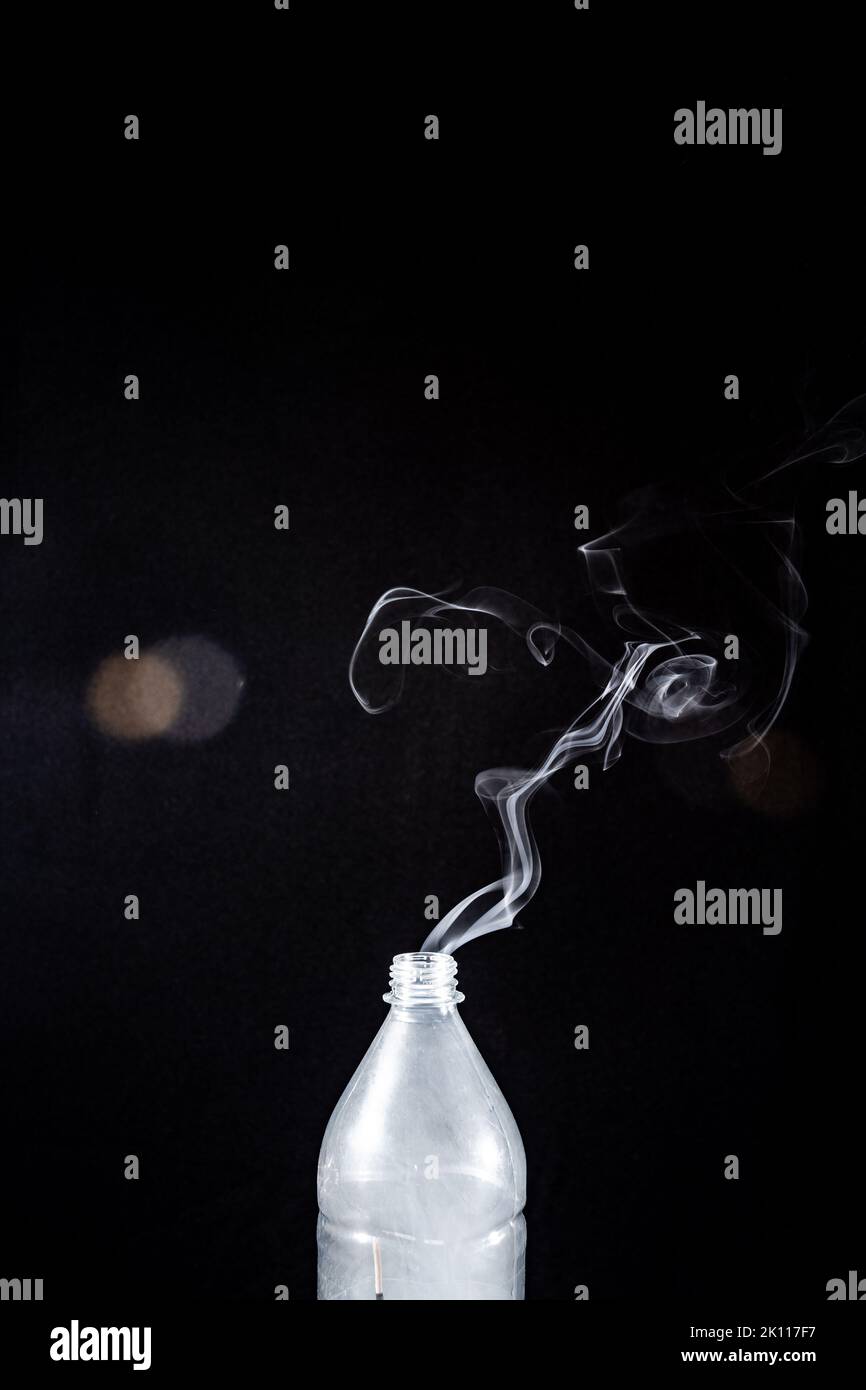 Smoke coming out of a plastic bottle against a black background with ...