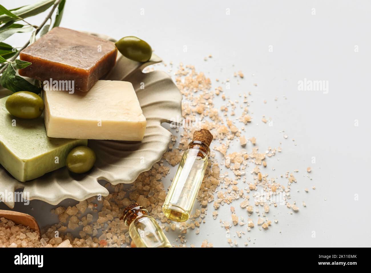 Plate with olive soap bars and bottle of essential oil on white ...