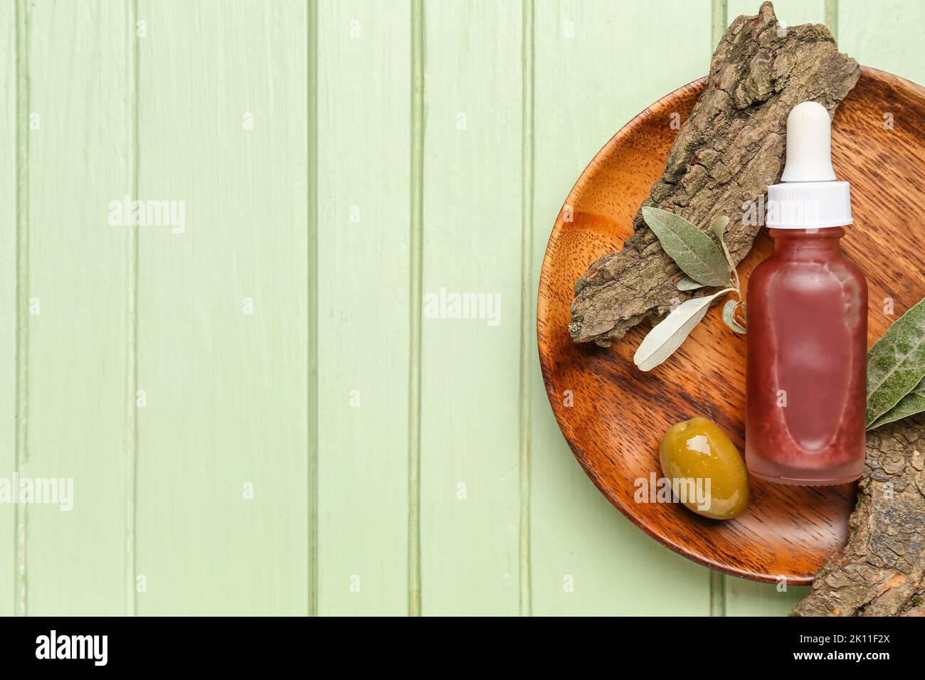Plate with bottle of essential olive oil on color wooden background ...