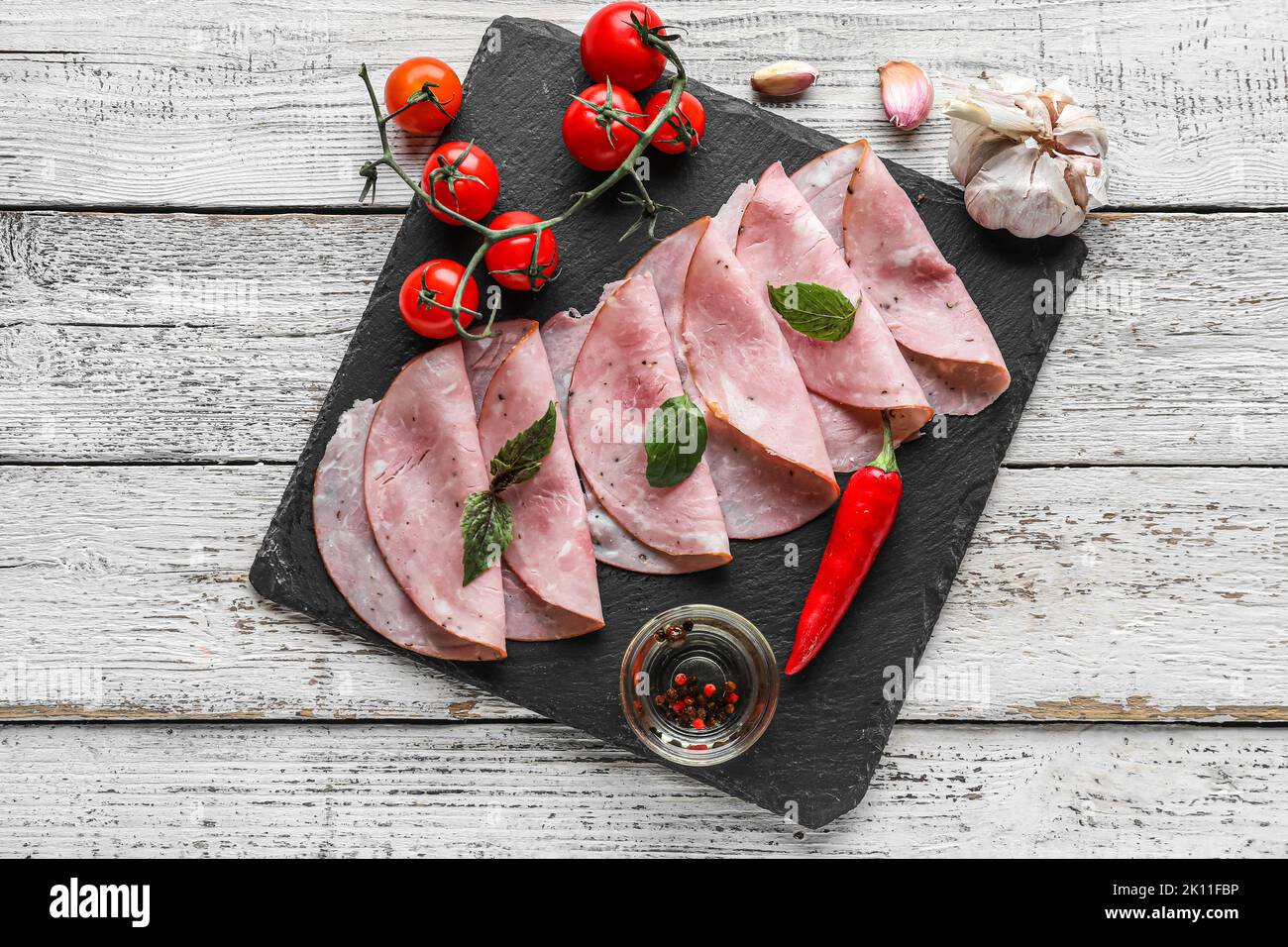 Board with slices of tasty ham, tomatoes and spices on light wooden ...
