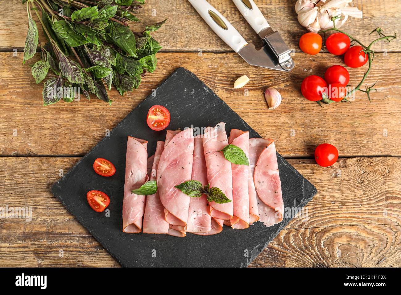 Board with slices of tasty ham, tomatoes and basil on wooden background ...