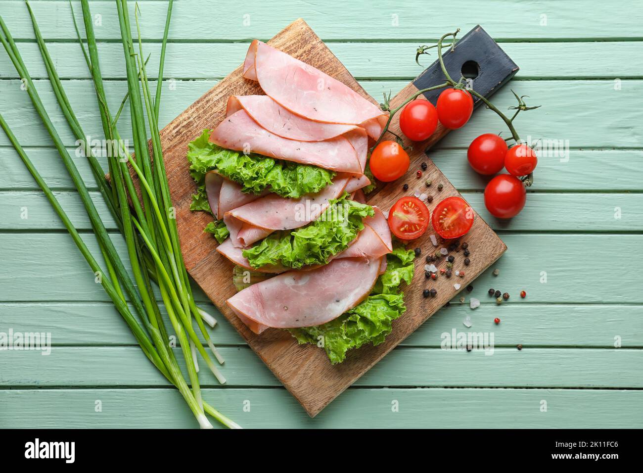 Board with slices of tasty ham, lettuce, tomatoes and green onion on ...