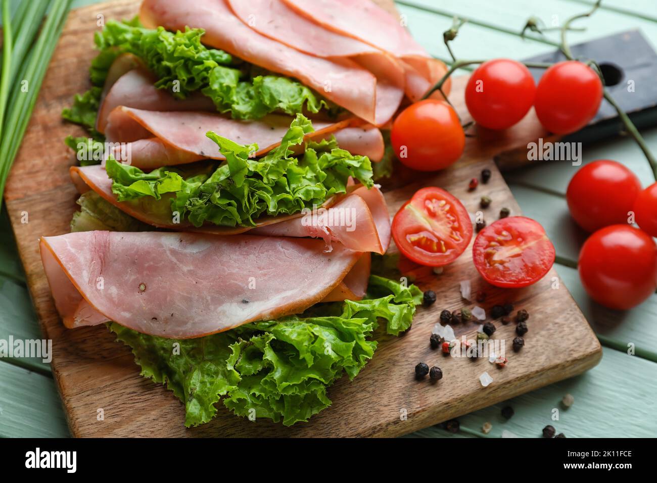 Board with slices of tasty ham, lettuce and tomatoes on color wooden ...
