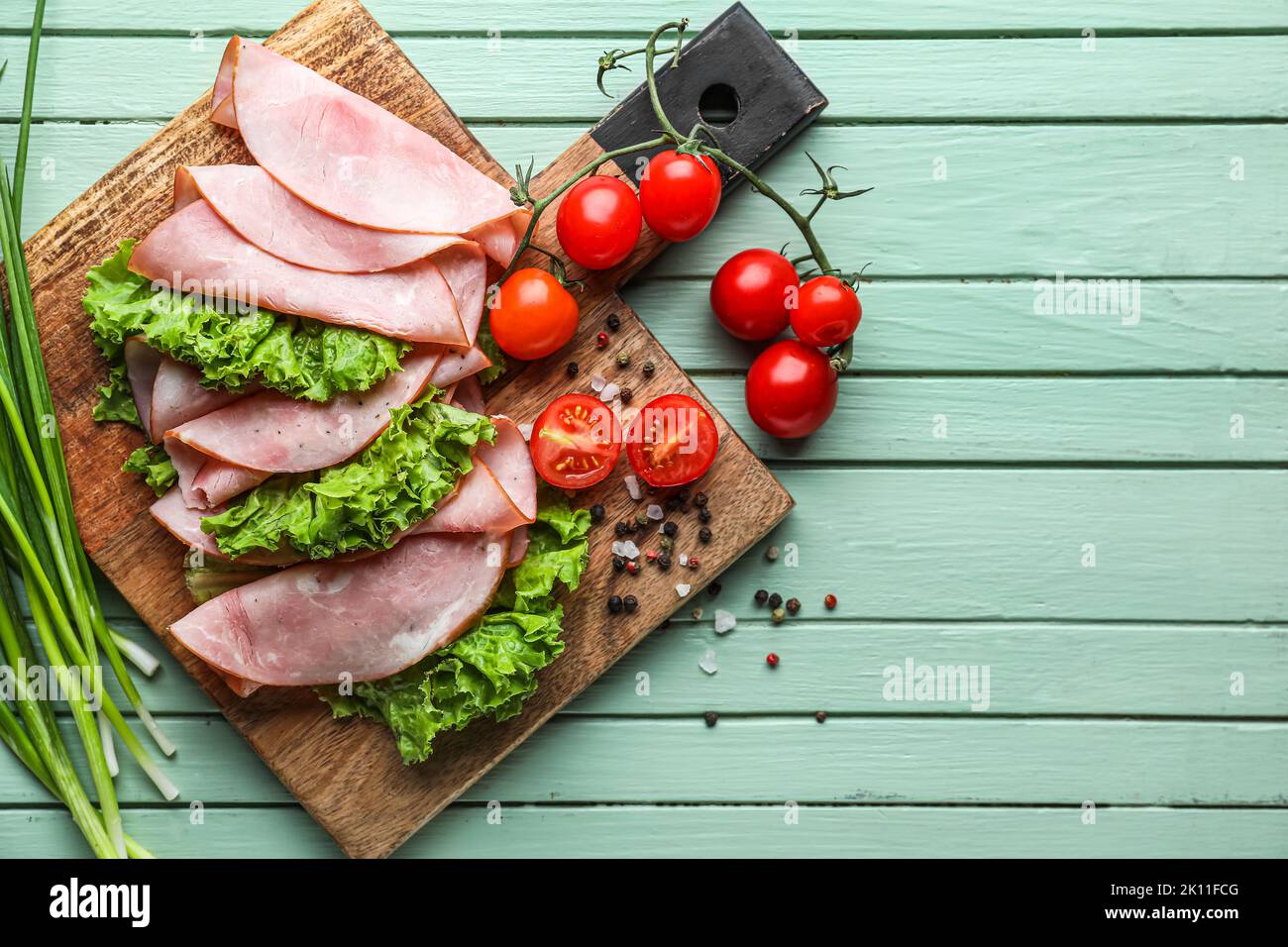 Board with slices of tasty ham, lettuce and tomatoes on color wooden ...
