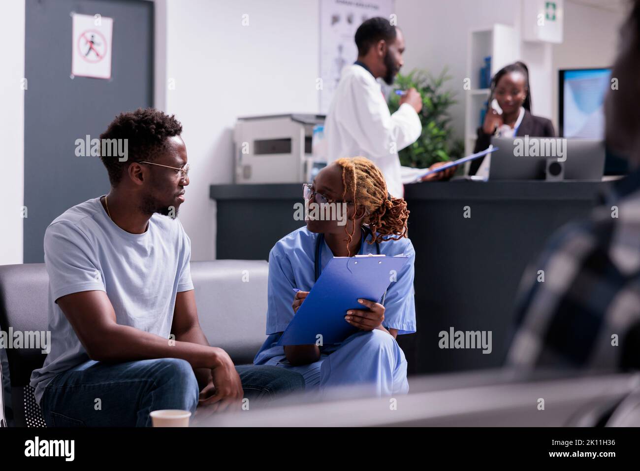 Medical assistant examining young man in waiting area lobby, taking ...