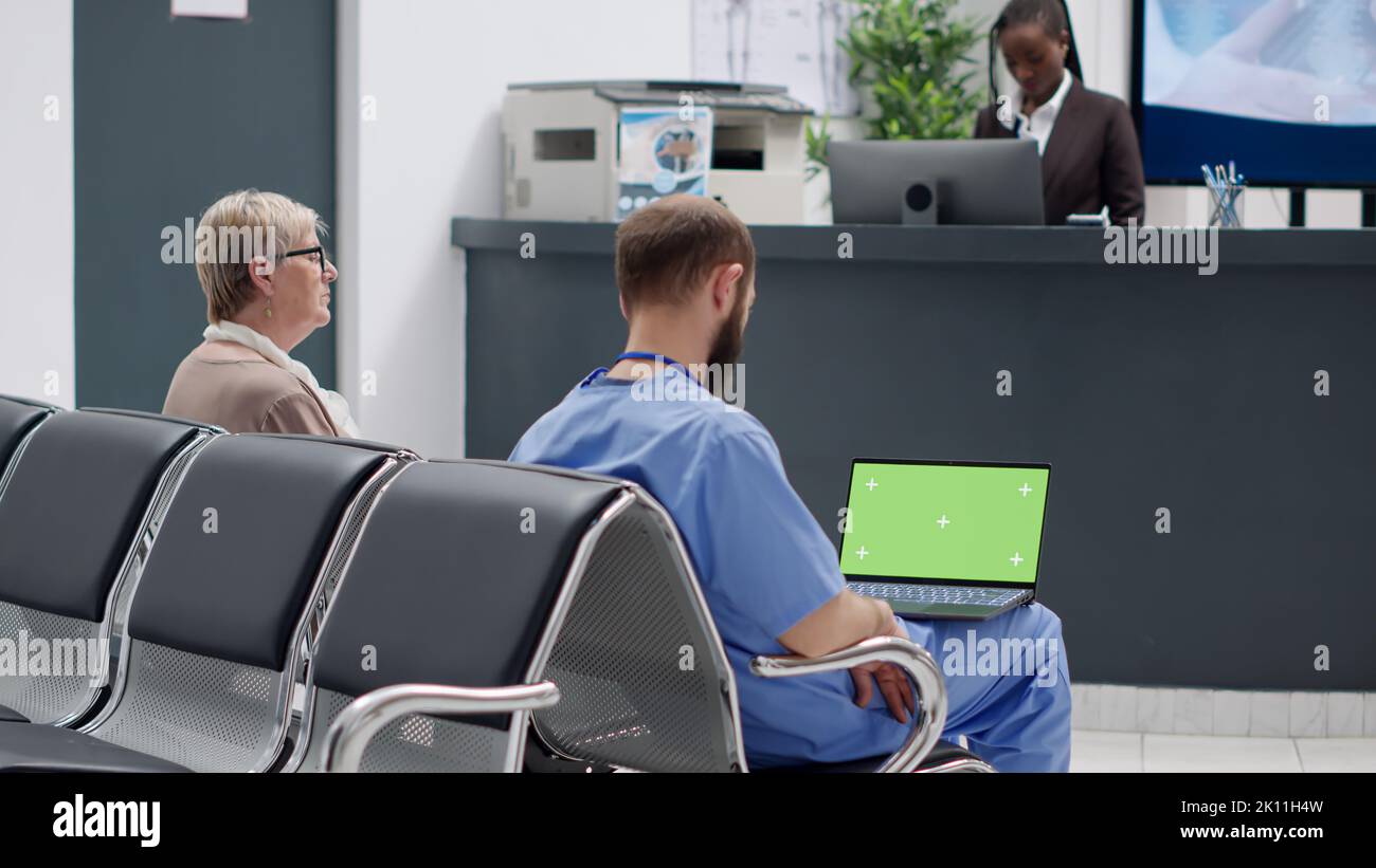 Male nurse analzying greenscreen display on laptop in waiting room ...