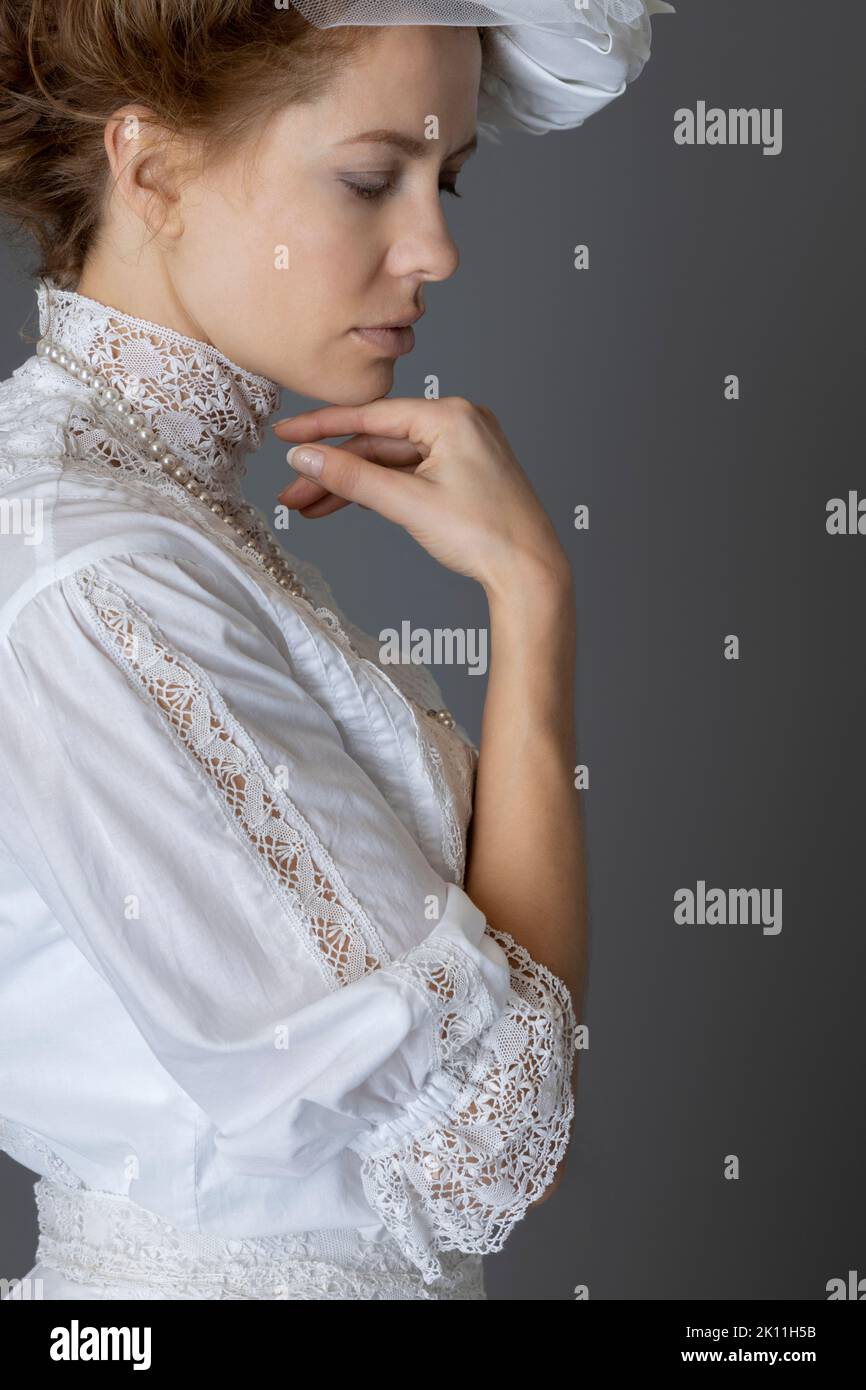 An Edwardian woman wearing a white lace blouse and skirt against a grey ...