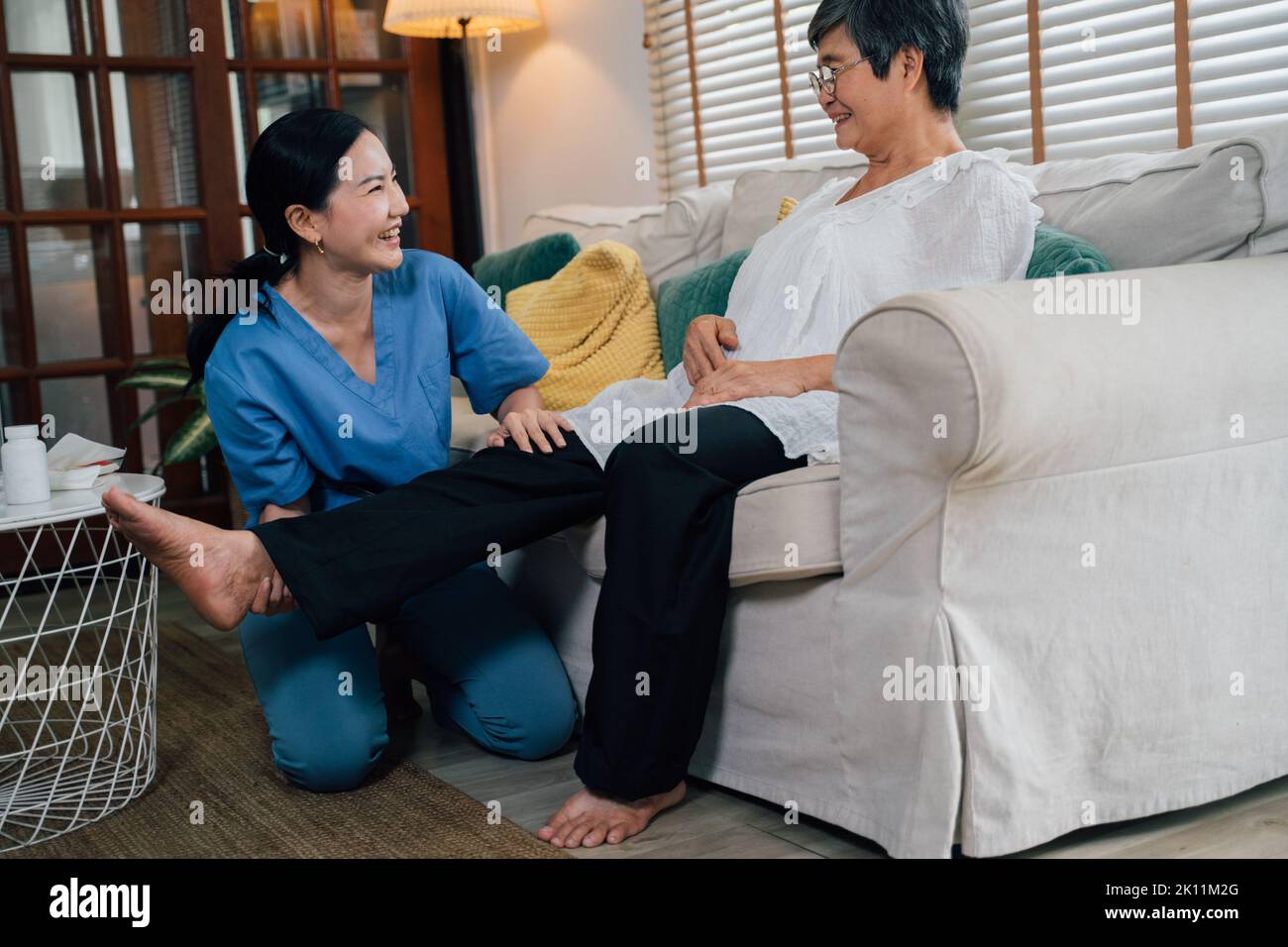 Happy Asian Female Caregiver Smiling And Stretching Leg Of Elderly