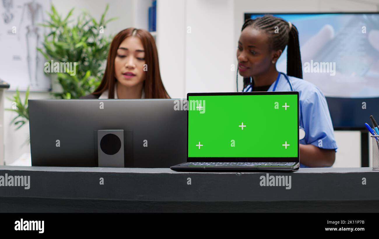 Diverse receptionist and nurse working with greenscreen on laptop at ...
