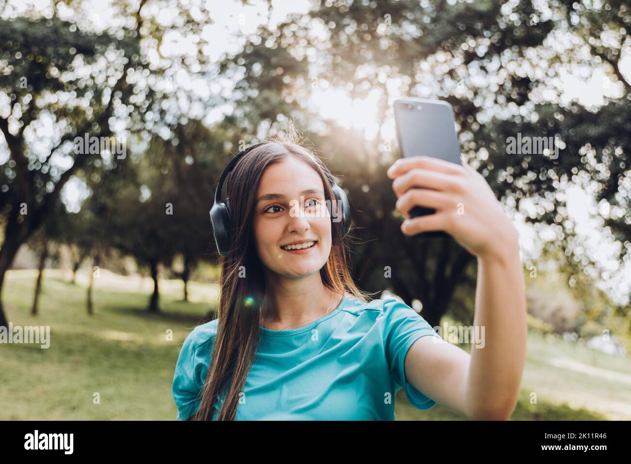 Smiling teenage girl wearing a turquoise t shirt and headphones, taking ...