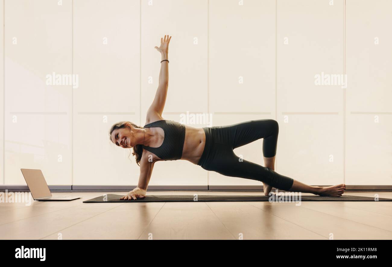 Senior woman doing a side angle pose during an online yoga class at ...