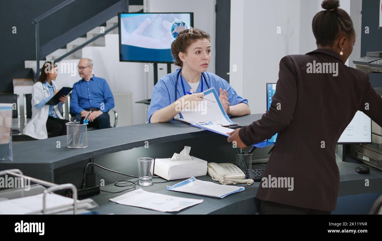 Nurse and receptionist analyzing checkup papers at reception counter ...