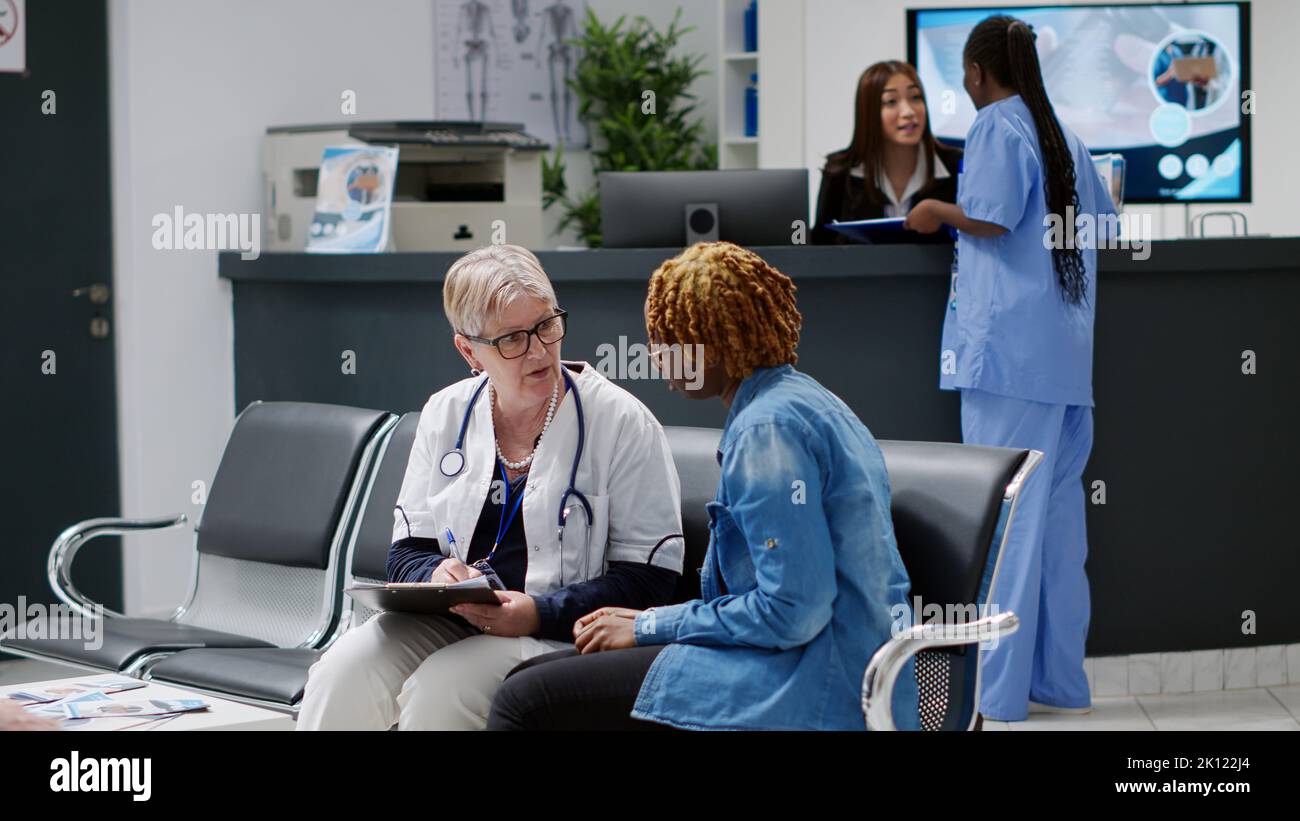 Old general practitioner taking notes at consultation with patient ...