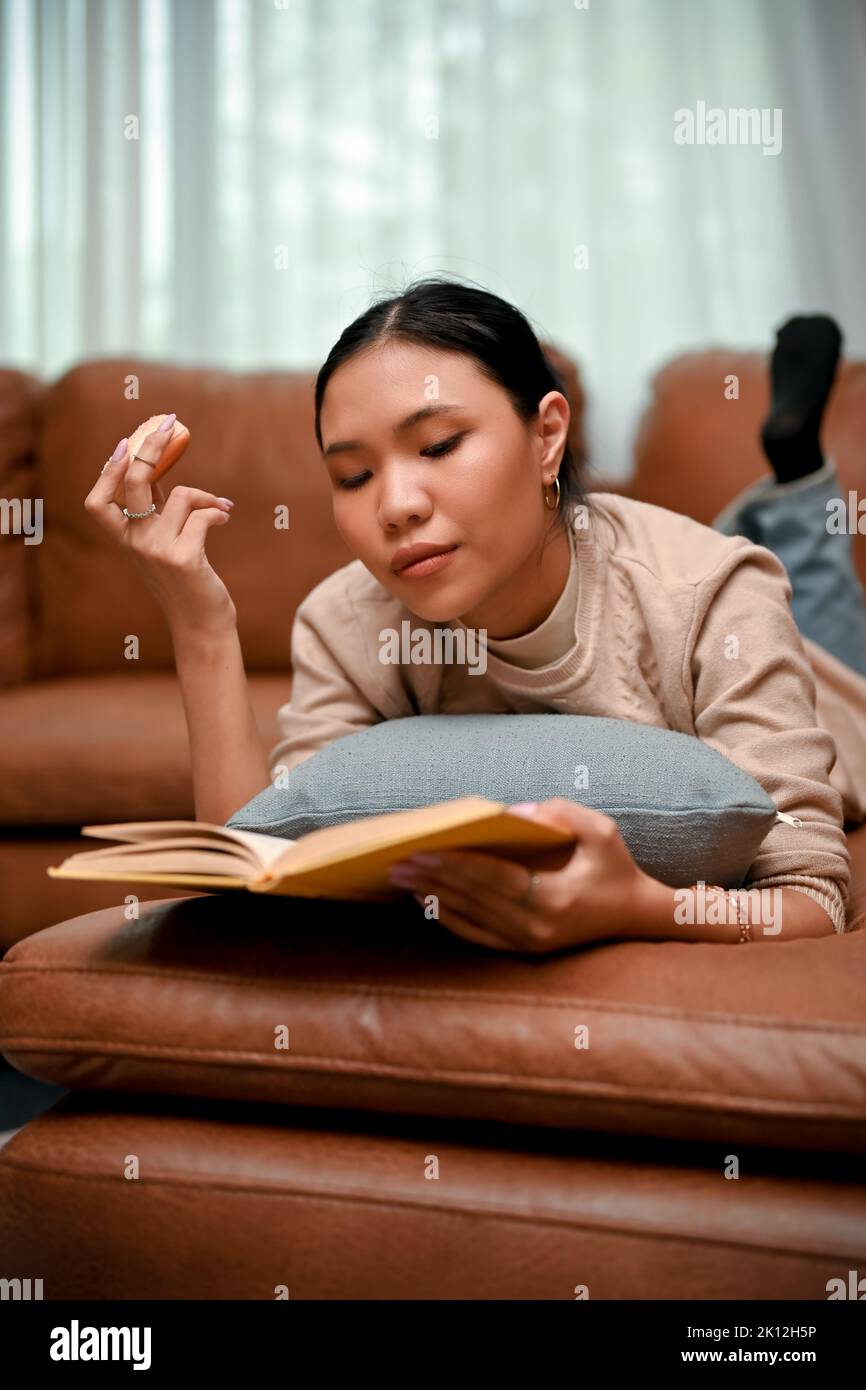 Portrait, Beautiful young Asian female snacking and reading a book ...
