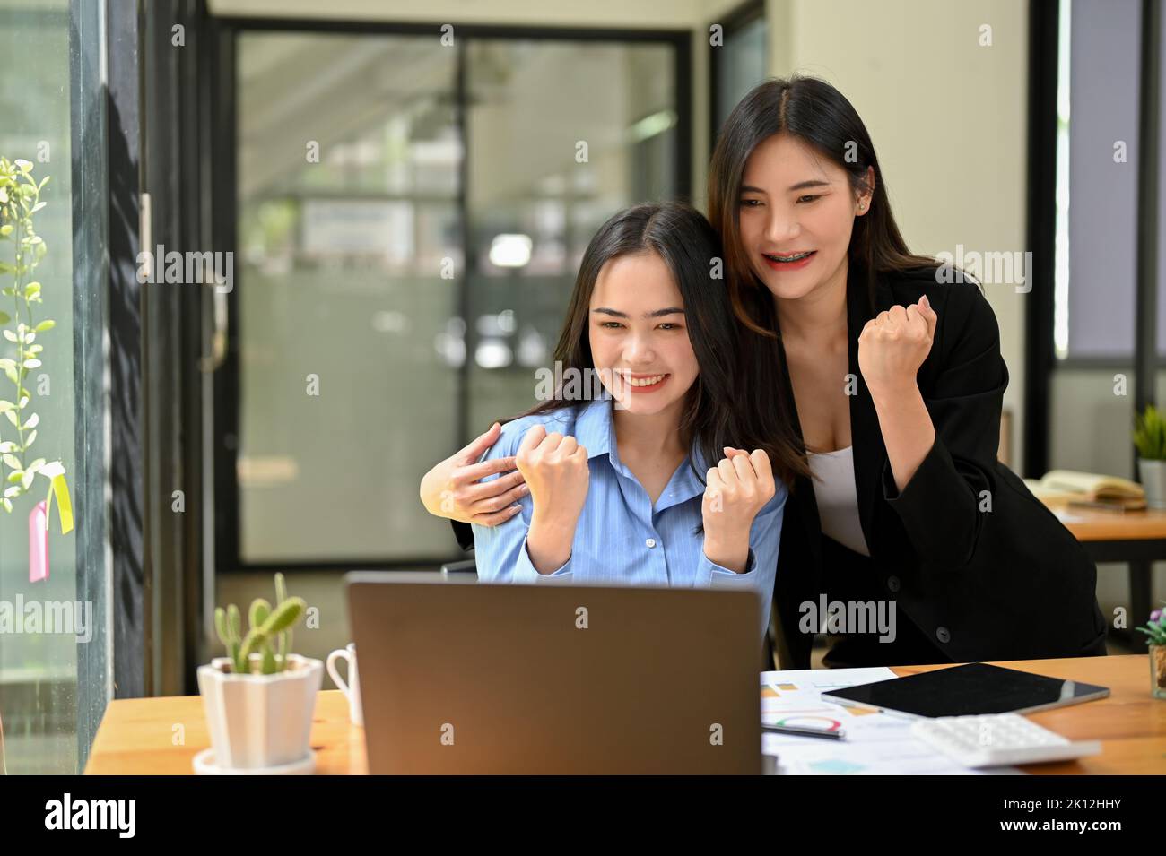 Cheerful young Asian businesswomen at the office desk, making cheer up ...