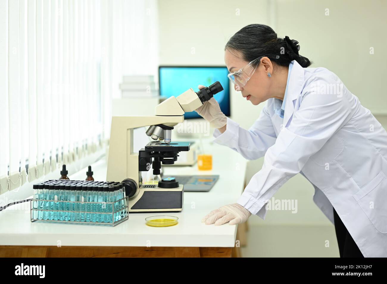 Senior woman biotechnology specialist looking under microscope ...