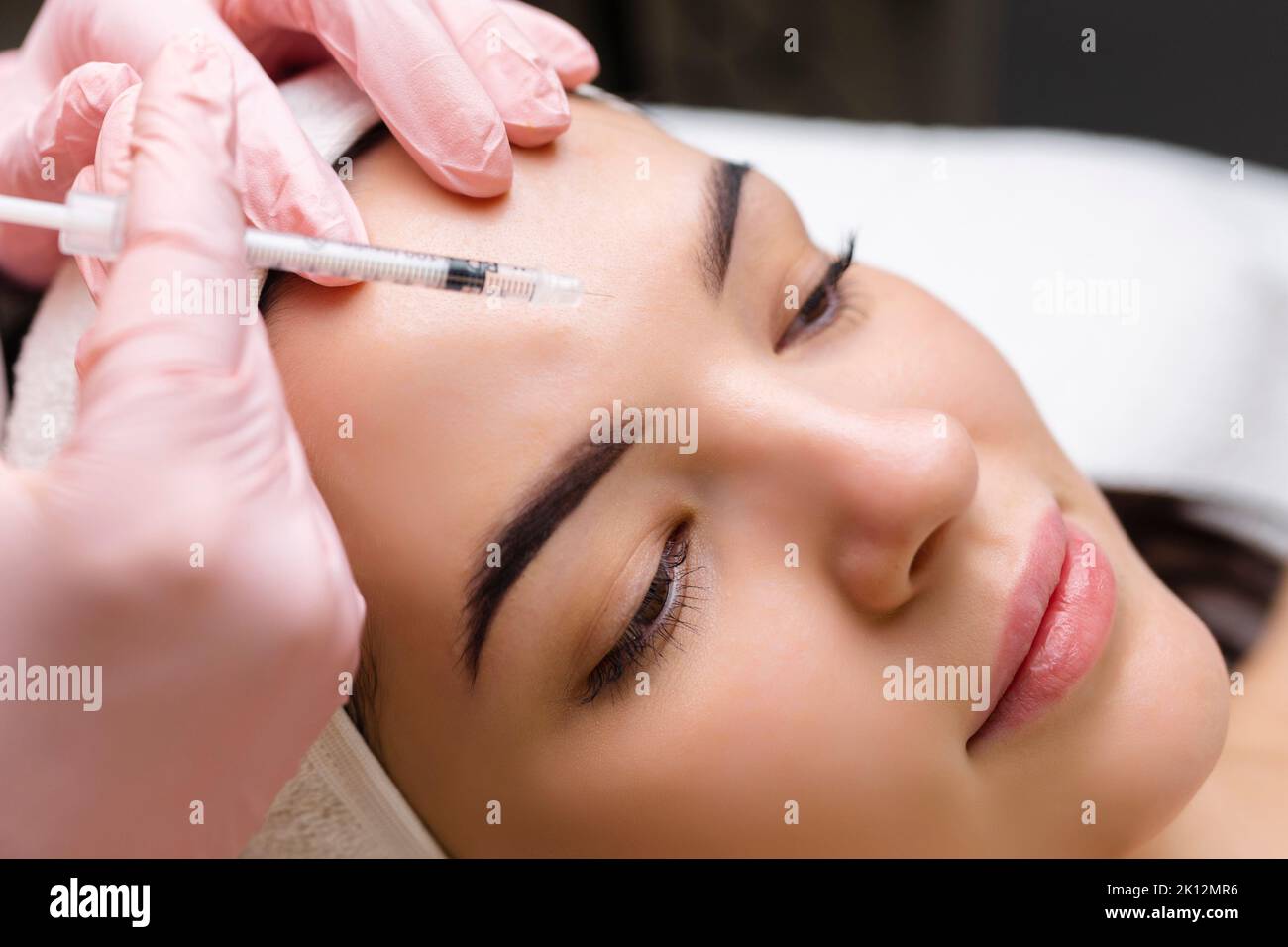 Close up of hands of young cosmetologist injecting botox in female face ...