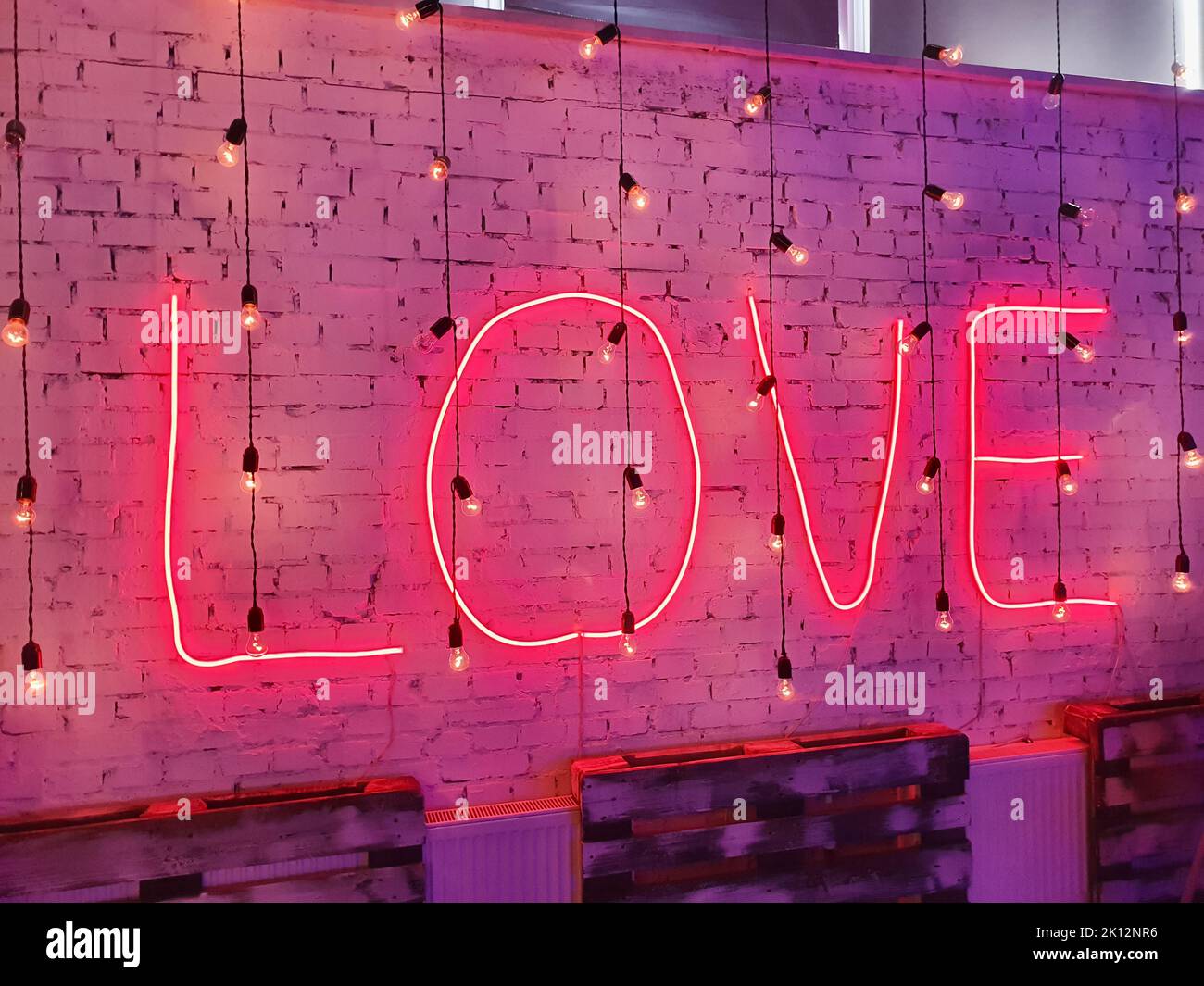 Pink crimson neon light lettering "Love" and lighted retro light bulbs ...