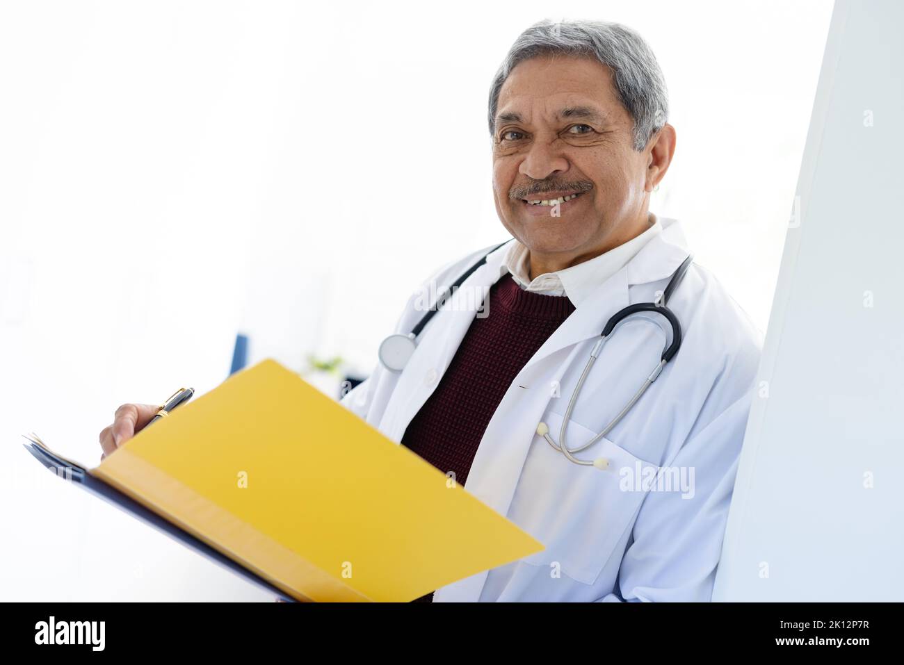 Portrait of smiling senior biracial male doctor holding patient file ...