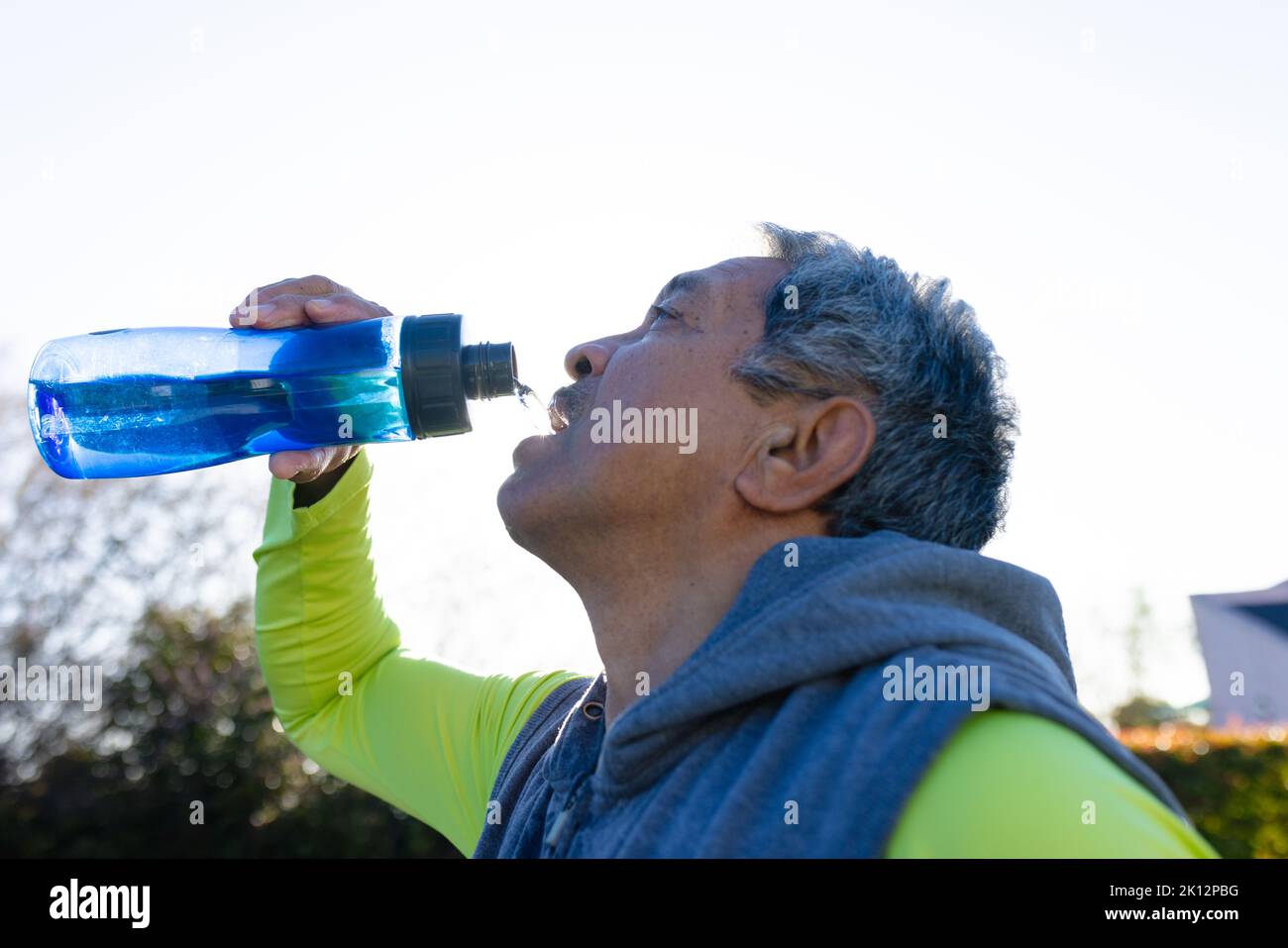Thirsty senior biracial man in sports clothes drinking water while out ...