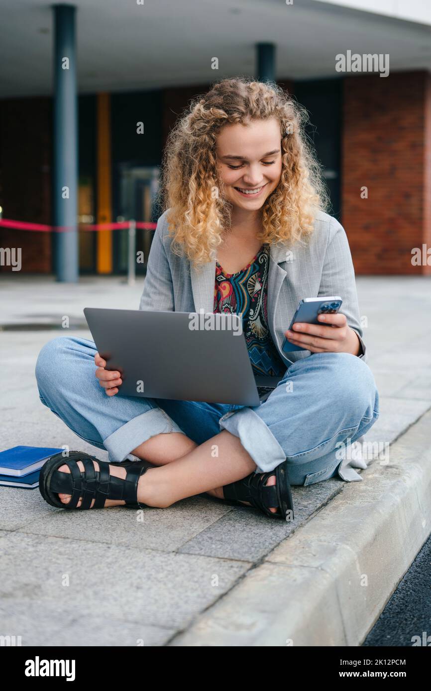 Smiling caucasian girl sitting in a street working at the computer ...