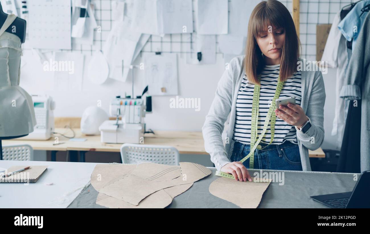 Young seamstress is checking clothing paper patterns and measuring them ...